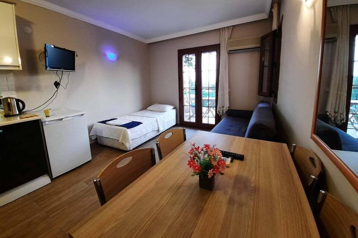 Quarto de hotel compacto com cozinha compacta, mesa de jantar, duas camas de solteiro, sofá e TV fixada na parede.