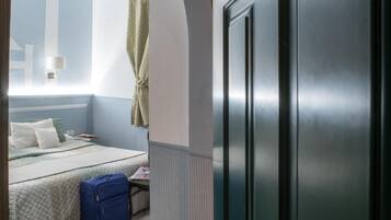 Quarto de hotel com uma cama, uma mala e uma porta com placa de número.