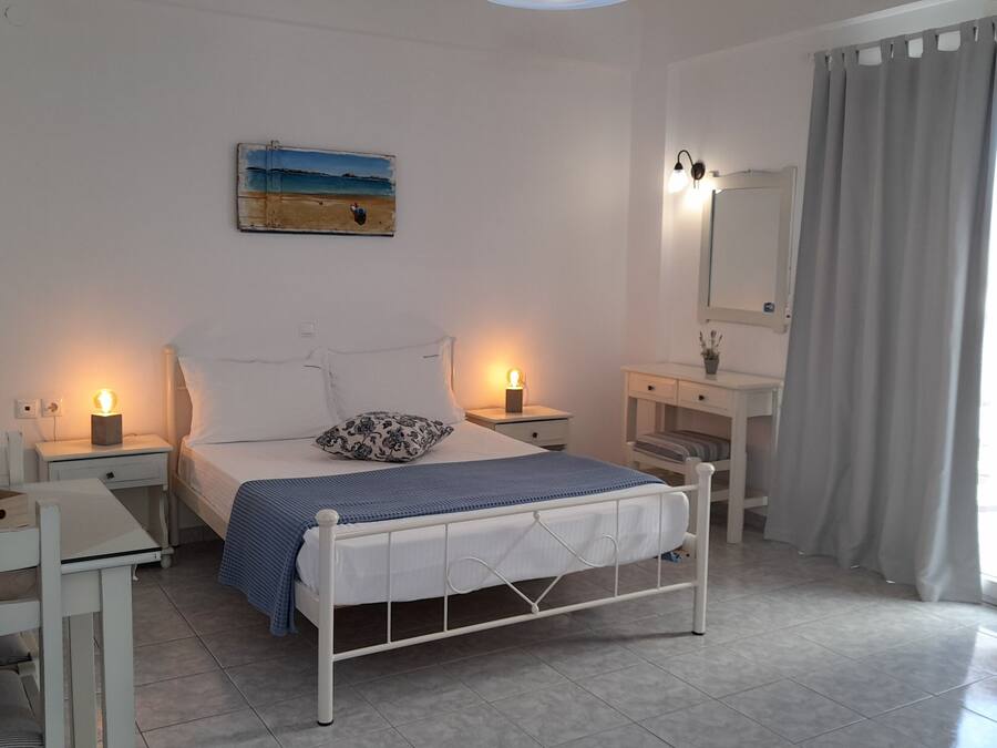 Quarto com cama, mesas de cabeceira, penteadeira, espelho e vista para o exterior.