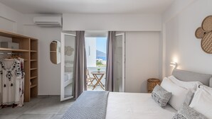 Quarto com cama, guarda-roupa, banheiro e varanda com vista para o mar.