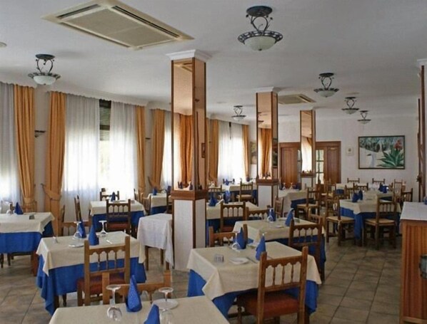 Espaço de refeições de hotel com várias mesas preparadas para jantares, com toalhas de mesa azuis e cadeiras de madeira.