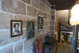 Paredes de pedra com retratos emoldurados, um banco e uma mesa com um vaso.