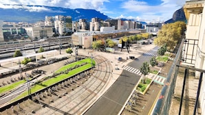 Um edifício alto com vista para um horizonte urbano, incluindo uma estação de trem e montanhas ao fundo.