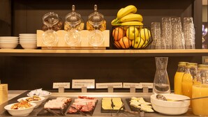 Buffet com diversos alimentos e bebidas, incluindo frutas, queijos e carnes.