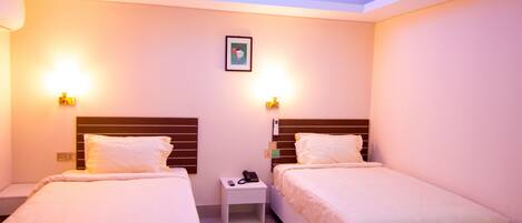Quarto de hotel com duas camas, mesa de cabeceira com telefone e luminária, e quadro pendurado na parede.