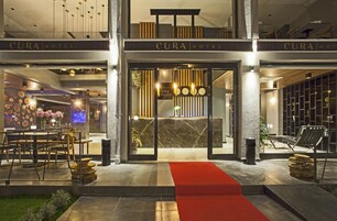 Entrada do Hotel CURA, com tapete vermelho, balcão de recepção em mármore e decoração moderna.