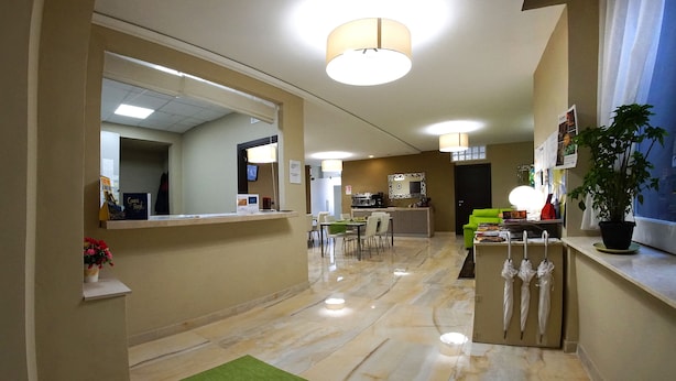 Um saguão de hotel com uma mesa de recepção, área de refeições e uma cozinha ao fundo.