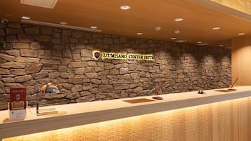 Uma mesa de recepção com parede de pedra ao fundo e uma placa com a inscrição "IZUMISANO CENTER HOTEL".