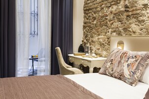 Quarto de hotel com cama, secretária, cadeira e parede de pedra.