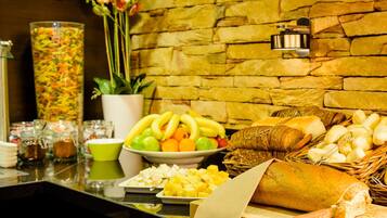 Disposição de buffet com diversos alimentos, incluindo frutas, pão e acompanhamentos.