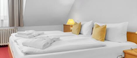 Quarto de hotel com cama bem arrumada, abajur e mesa de cabeceira de madeira.