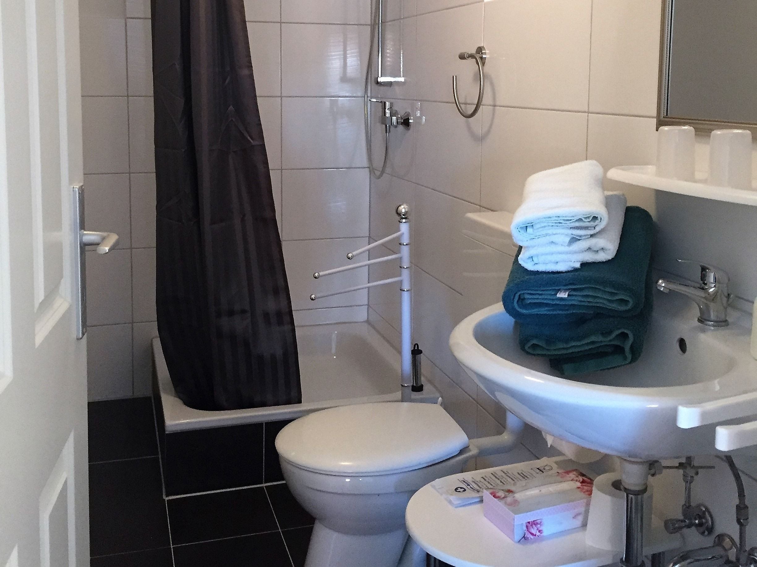 Casa de banho com sanita, lavatório, chuveiro e porta-toalhas.