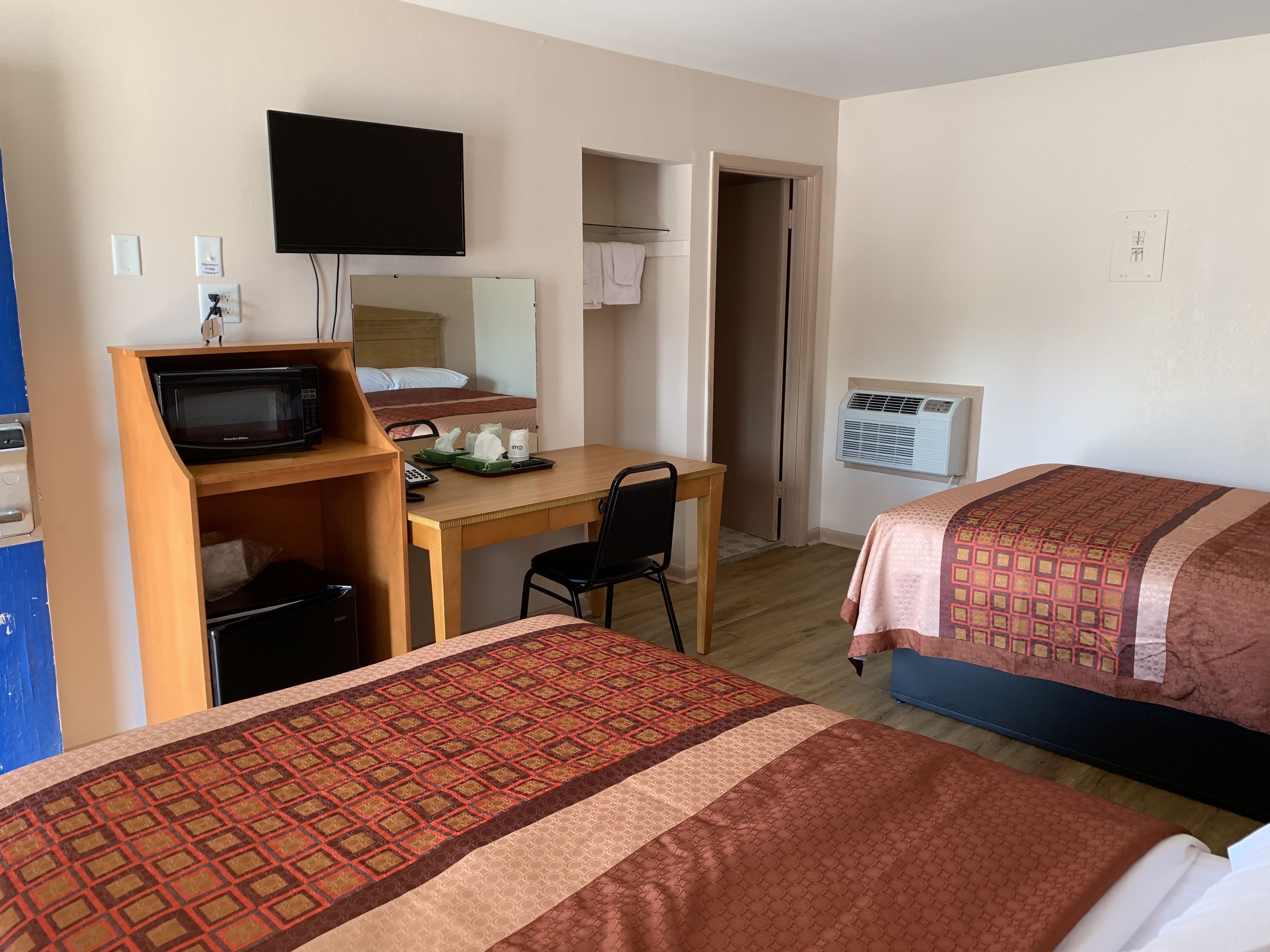 Quarto de hotel com escrivaninha, televisão, cama com roupa de cama estampada, cadeira e guarda-roupa.