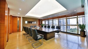 Uma sala de conferências moderna com uma mesa grande, cadeiras pretas e amplas janelas com vista para a cidade.