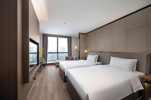 Quarto de hotel com duas camas, uma janela grande, uma varanda e uma escrivaninha com cadeira.