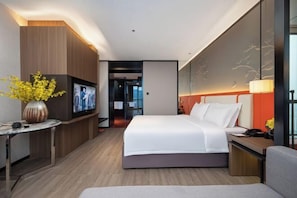 Quarto de hotel moderno com uma cama grande, uma televisão, uma escrivaninha e um vaso de flores.