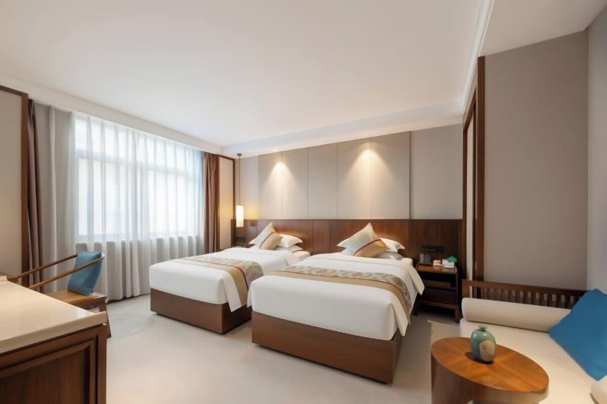 Quarto de hotel com duas camas, uma escrivaninha, uma cadeira e um sofá.