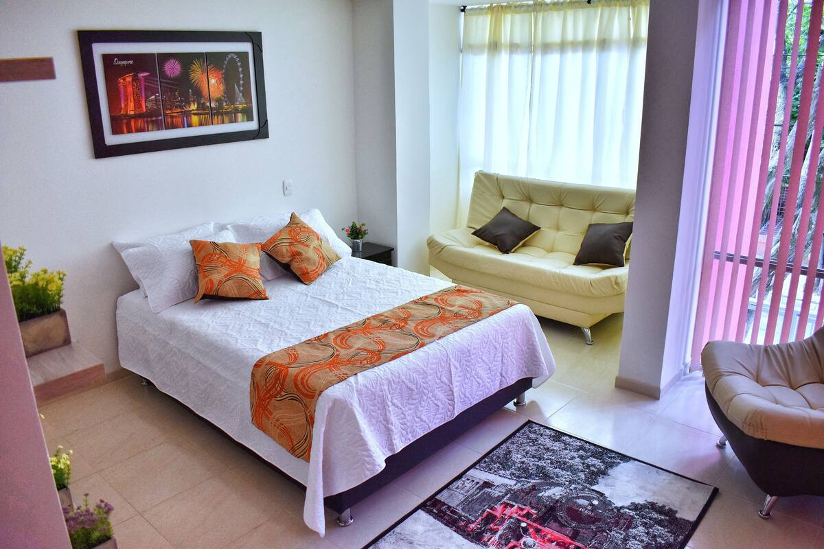 Quarto com cama, sofá e janela com cortinas.