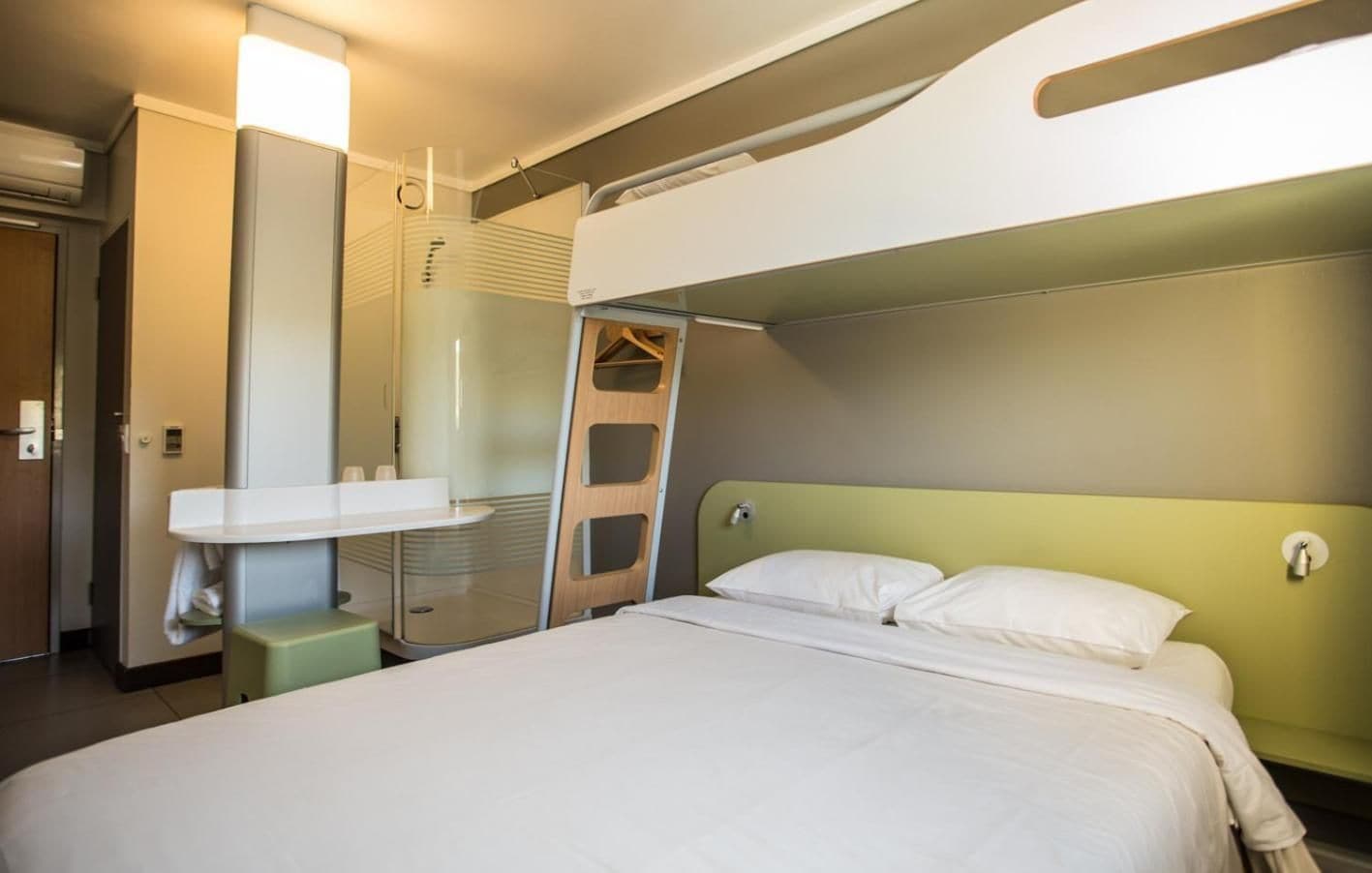 Quarto de hotel com cama, mesa de cabeceira, espelho e guarda-roupa.