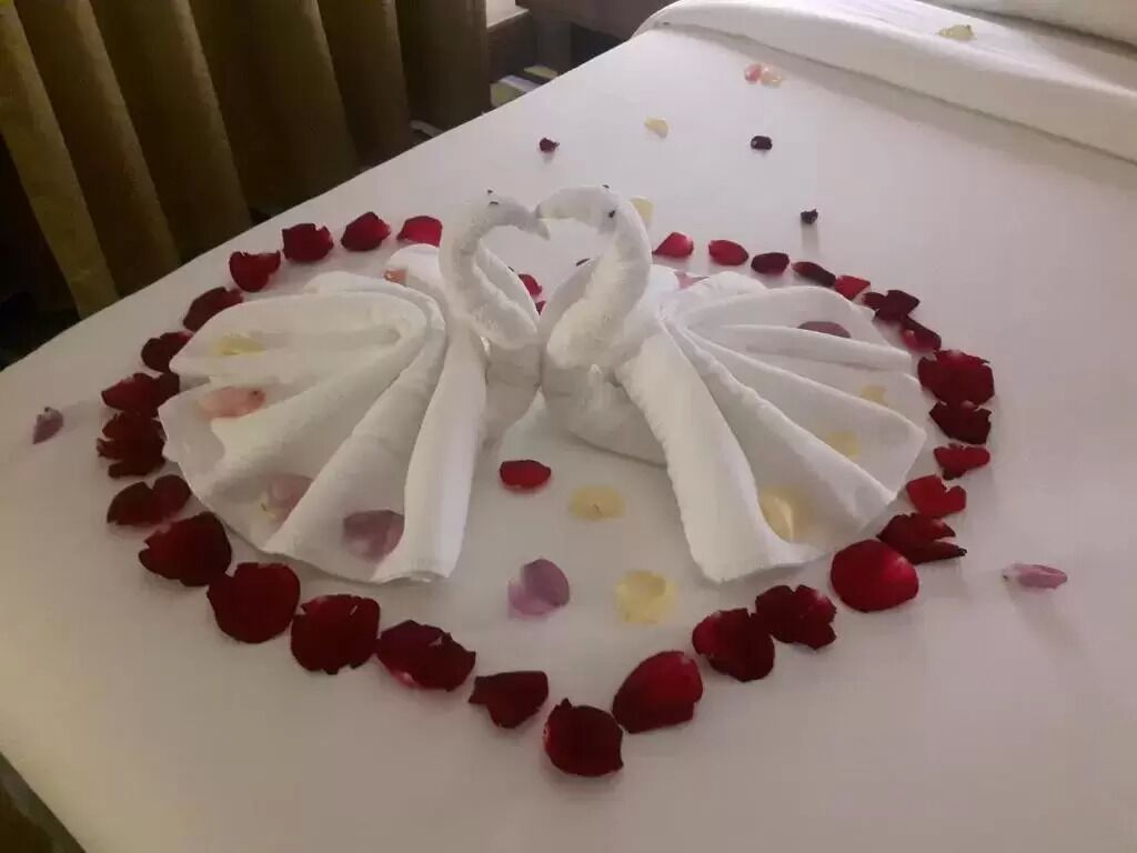 Cama com toalha disposta em formato de cisne, rodeada por pétalas de rosa.