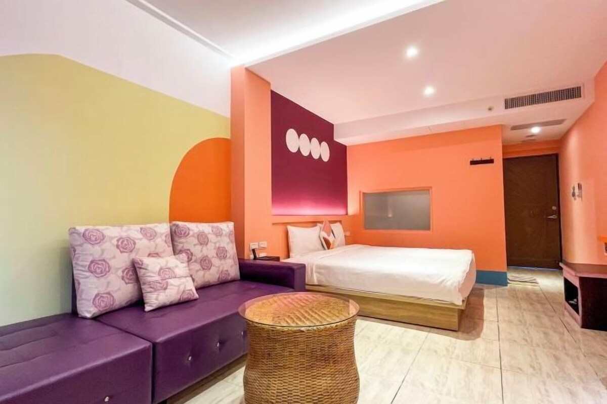 Quarto de hotel moderno com cama, sofá, televisão e uma obra de arte na parede.