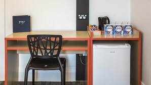 Um espaço de trabalho compacto com uma mesa, uma cadeira, um pequeno frigorífico e uma máquina de café.