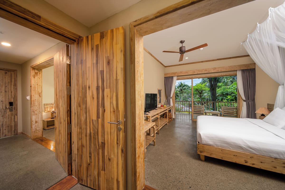 Quarto com cama de madeira, TV e varanda com vista para área verde.