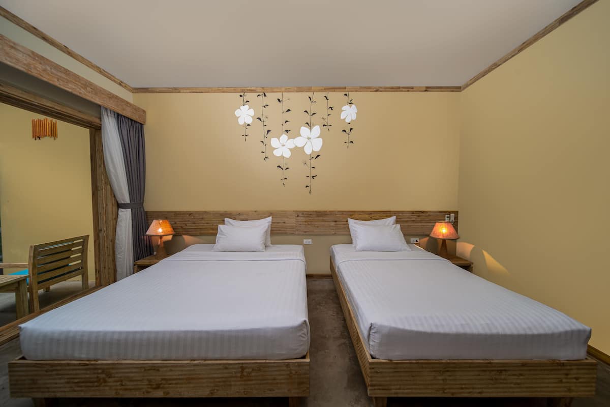 Quarto de hotel com duas camas de madeira, cabeceiras de madeira, um ornamento floral na parede e duas luminárias de cabeceira.