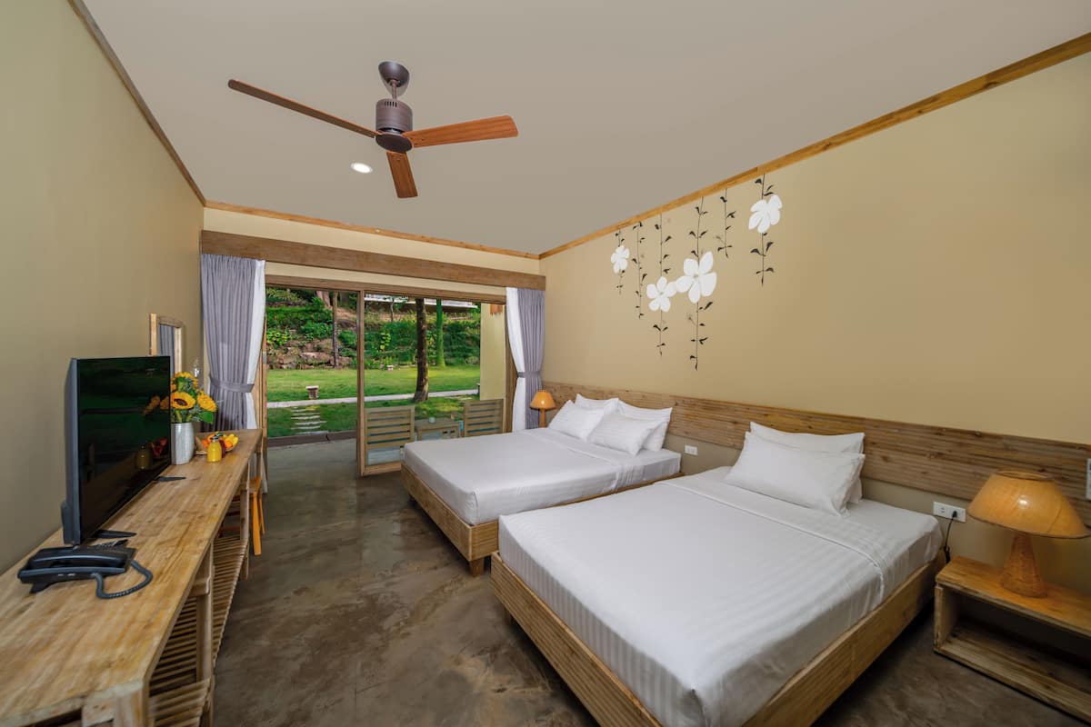 Quarto de hotel com duas camas, uma escrivaninha de madeira, uma televisão e um ventilador de teto.