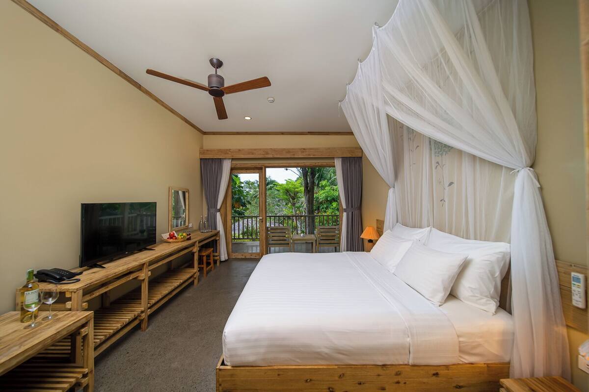 Um quarto com cama, escrivaninha, televisão e ventilador de teto.
