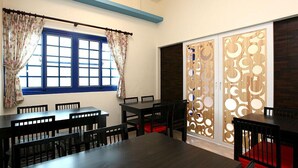 Uma sala de jantar com uma mesa comprida e várias cadeiras, uma janela com molduras azuis e uma divisória de madeira decorativa.