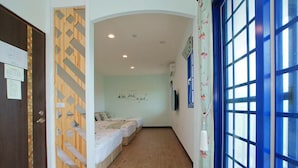 Corredor de hotel com piso de madeira, janela emoldurada por azul e parede com desenho decorativo.