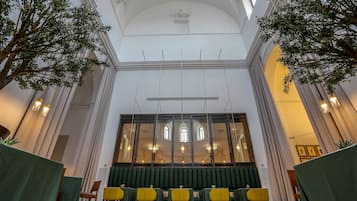 Uma área de refeições com teto alto, cadeiras estofadas em verde e uma fileira de mesas.