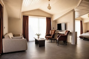 Quarto de hotel moderno com sofá, poltronas, televisão de tela plana e uma cama.