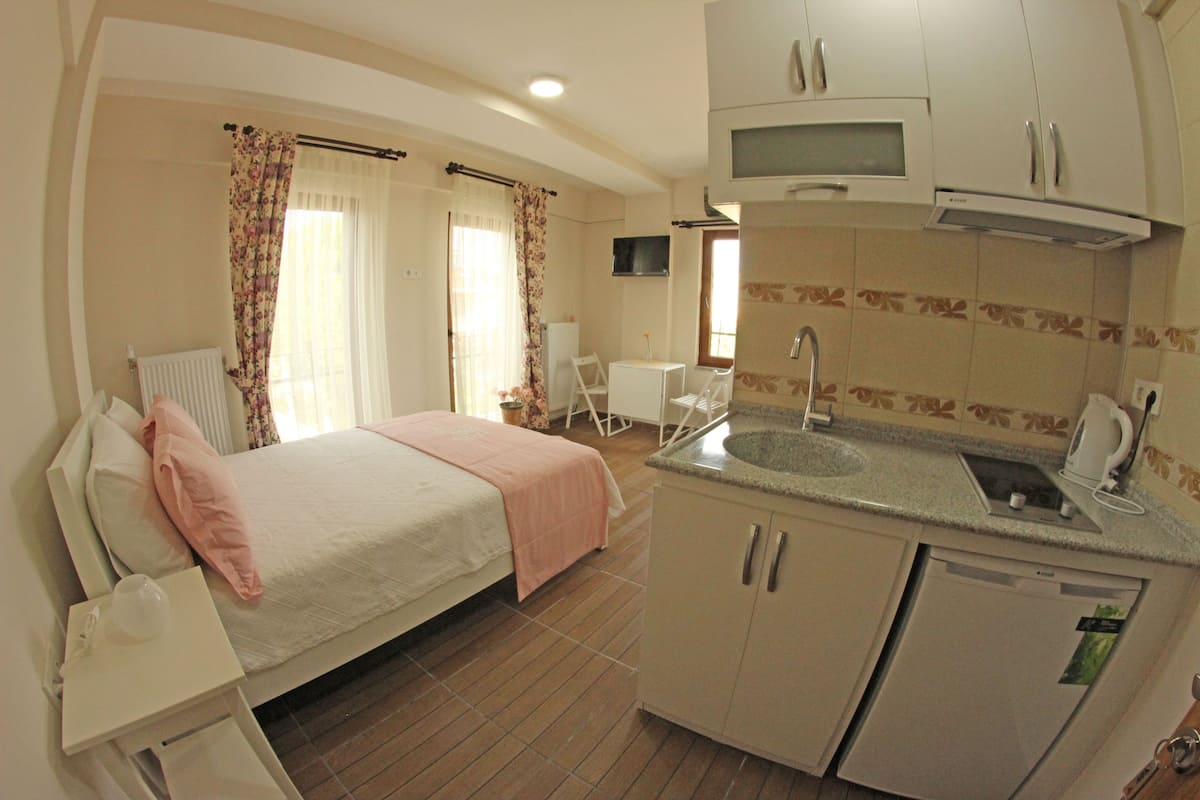 Quarto de hotel pequeno com uma cama, uma kitchenette, um banheiro e uma televisão.