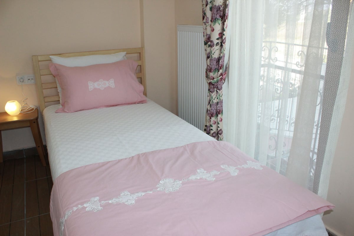 Um quarto com uma cama, uma mesa de cabeceira, um radiador e uma janela com cortinas.