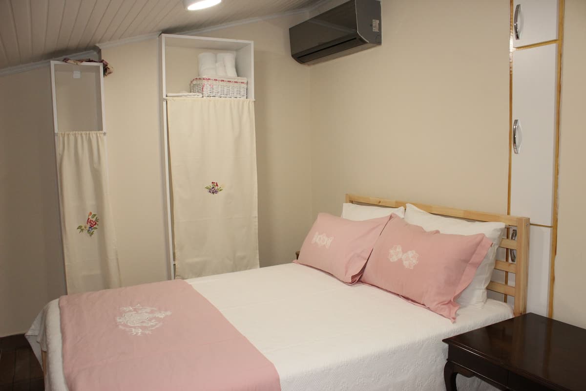 Quarto com cama, mesa de cabeceira de madeira, guarda-roupa e ventoinha no teto.