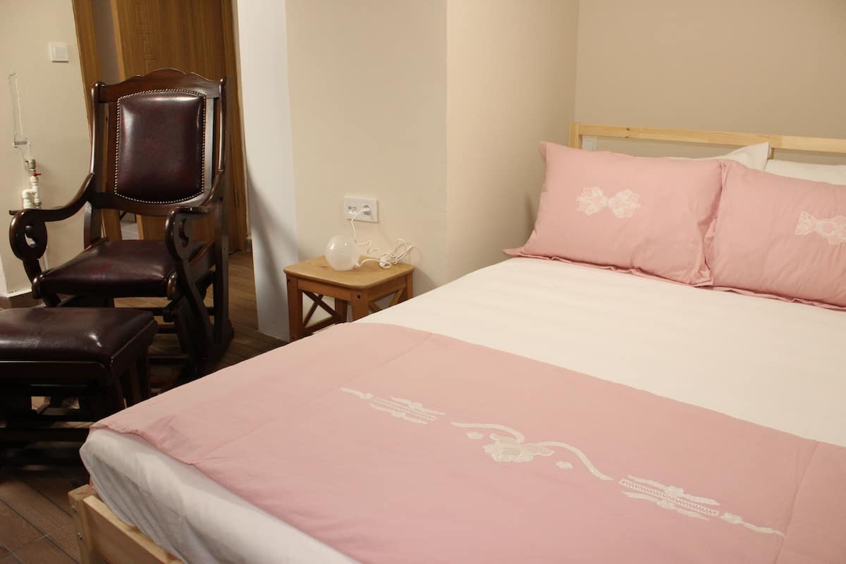Quarto com cama, uma cadeira de madeira, mesa de cabeceira e criado-mudo.