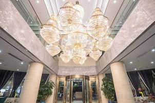 Um saguão com um grande lustre, colunas de mármore e entrada de vidro.