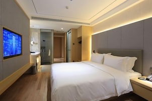 Quarto de hotel com uma cama grande, uma mesa de cabeceira, televisão na parede e banheiro visível através de uma porta aberta.