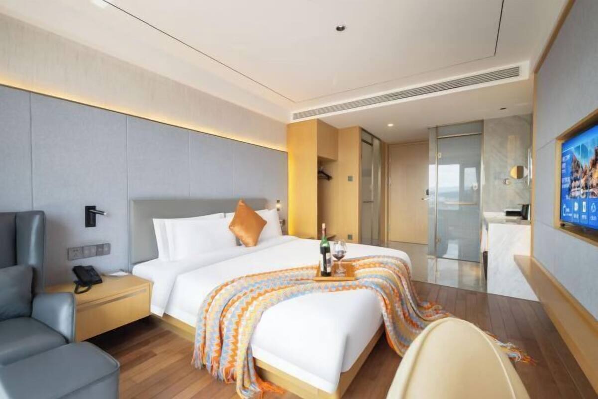 Quarto de hotel moderno com cama, mesa de cabeceira, cadeira e televisão.