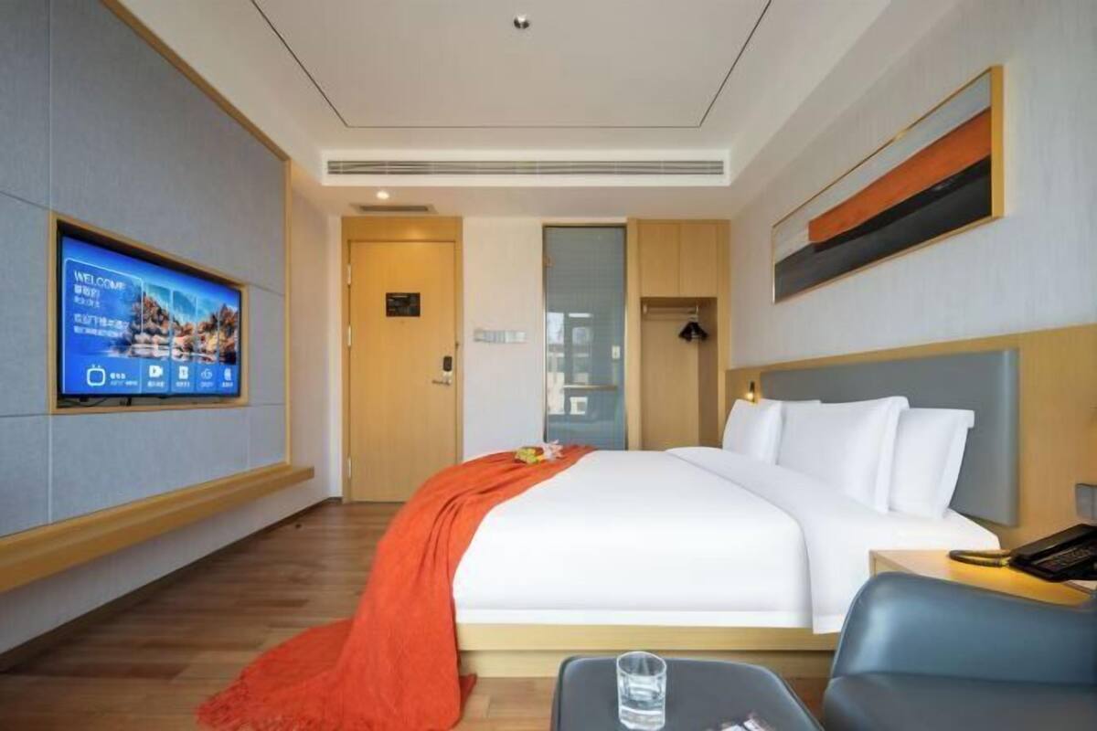 Quarto de hotel com cama, televisão na parede, escrivaninha e cadeira, e uma porta.