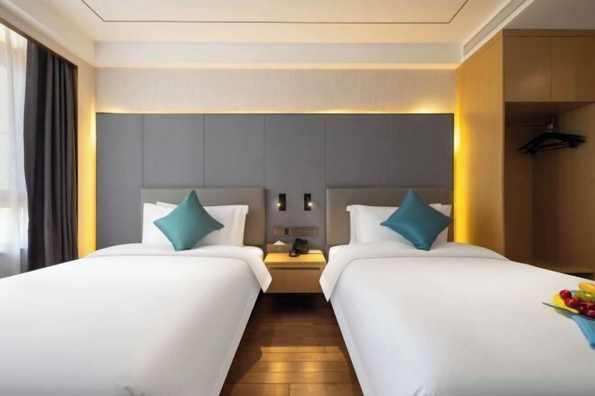 Quarto de hotel com duas camas, uma mesa de cabeceira, um telefone e uma pequena mesa com fruta.