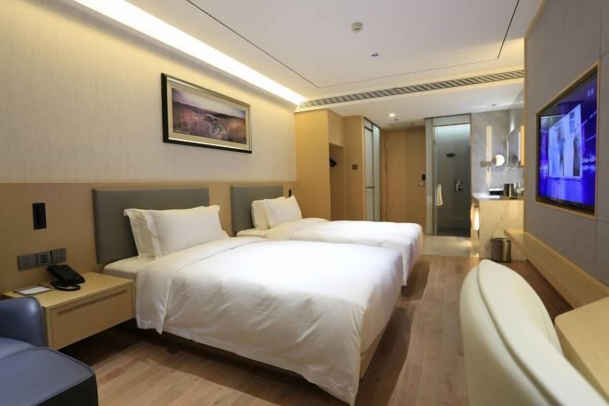 Quarto de hotel com duas camas, uma escrivaninha com telefone, televisão e um quadro na parede.