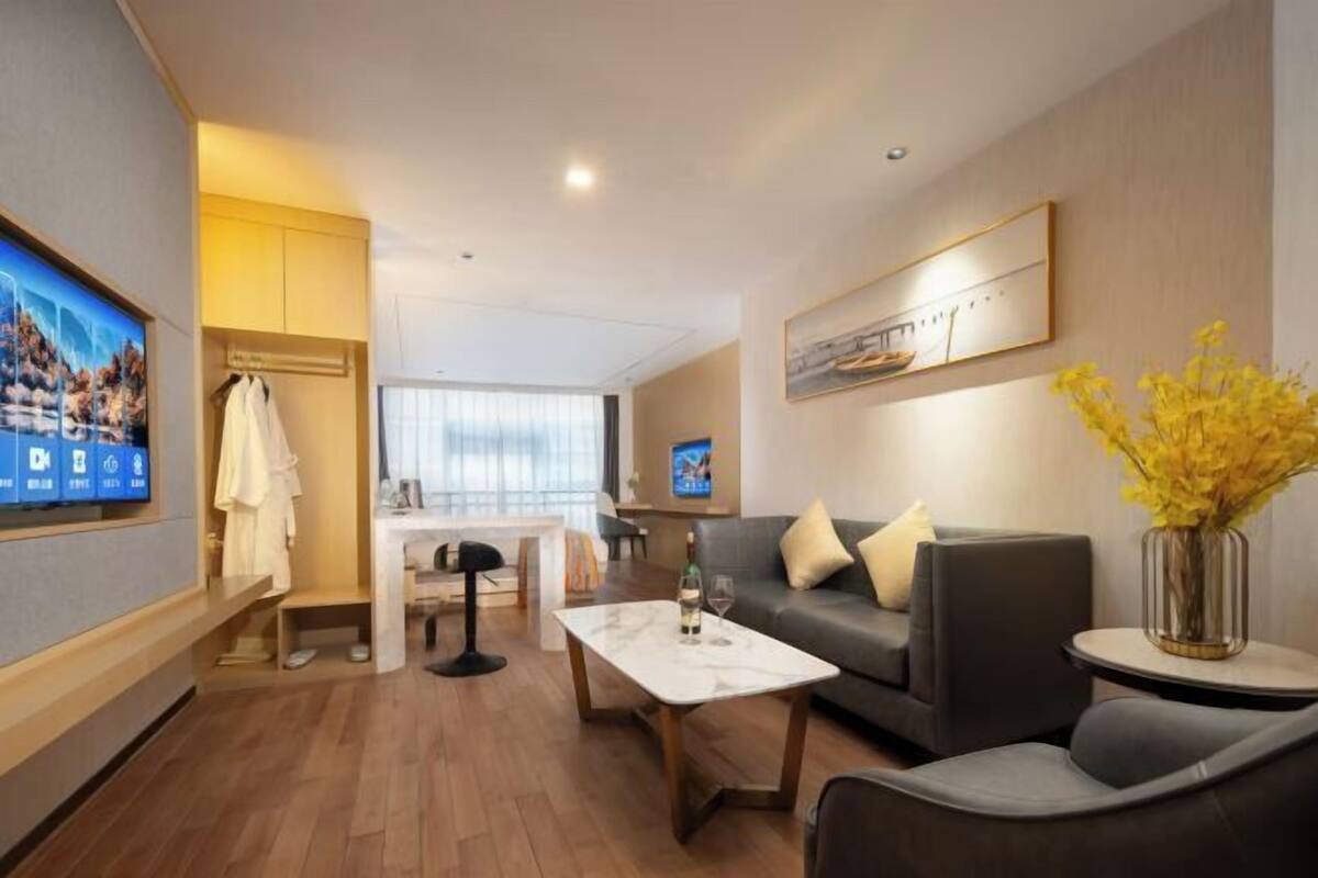 Quarto de hotel moderno com sofá, poltrona, mesa de centro e TV fixada na parede.
