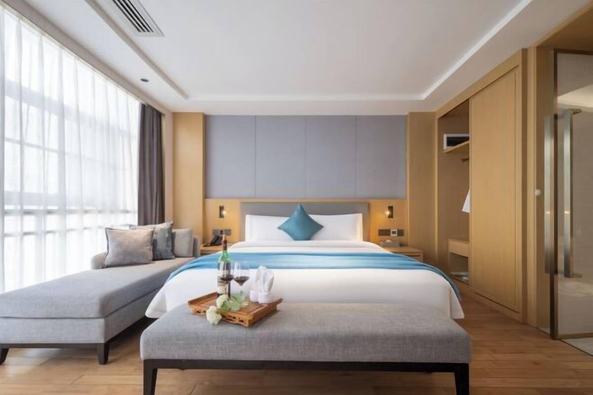Quarto de hotel moderno com uma cama grande, um sofá e uma bandeja de madeira com artigos de conveniência.