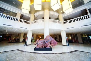 Um hall espaçoso com um pilar central, uma grande escultura e um teto alto com luminárias.