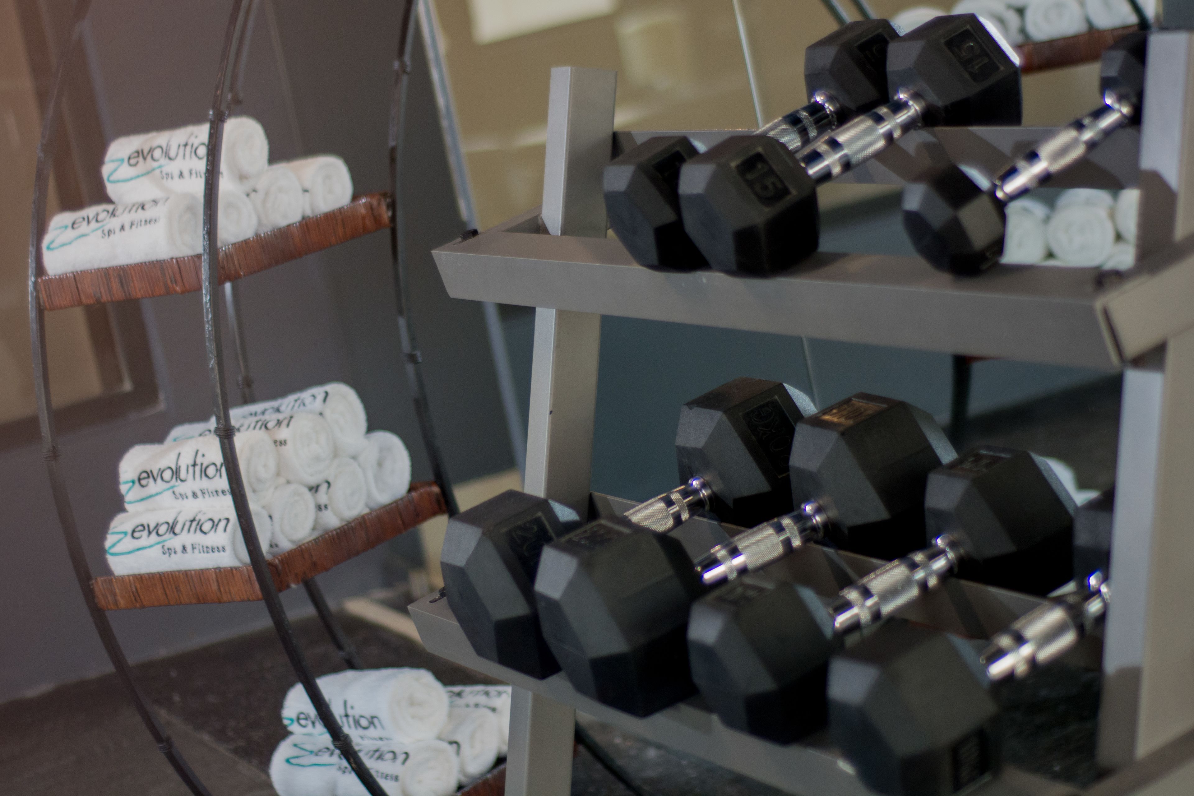 Um suporte com halteres organizados e toalhas enroladas, identificados como 'Evolution Spa & Fitness'.