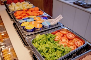 Buffet com diversos alimentos, incluindo frutas, vegetais e potes de iogurte.