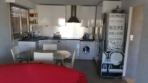 Cozinha compacta com máquina de lavar, mesa de jantar com cadeiras e frigorífico com design decorativo.